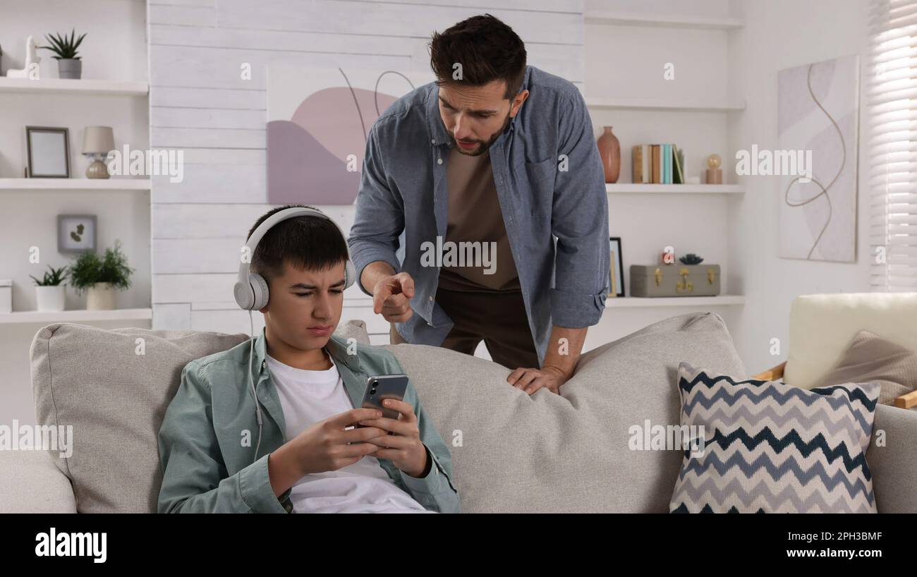 Father scolding his son while he listening music in headphones at home ...