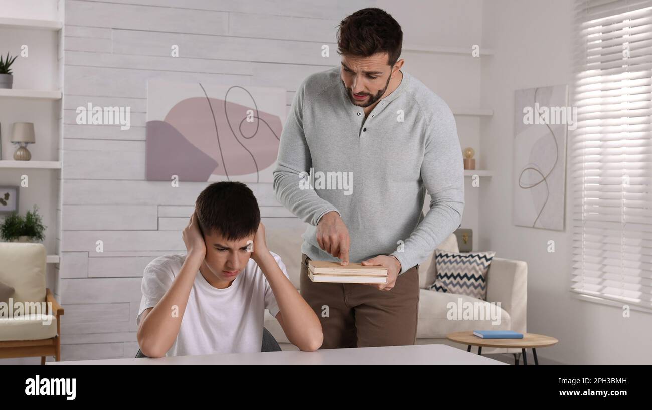 Strict father with books scolding his son at home. Teenager problems ...