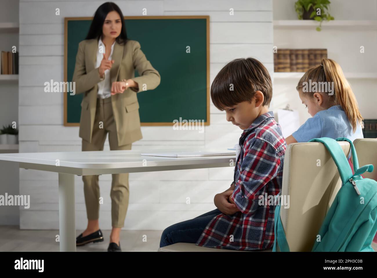 Teacher pointing on wrist watch while scolding pupils for being late in ...