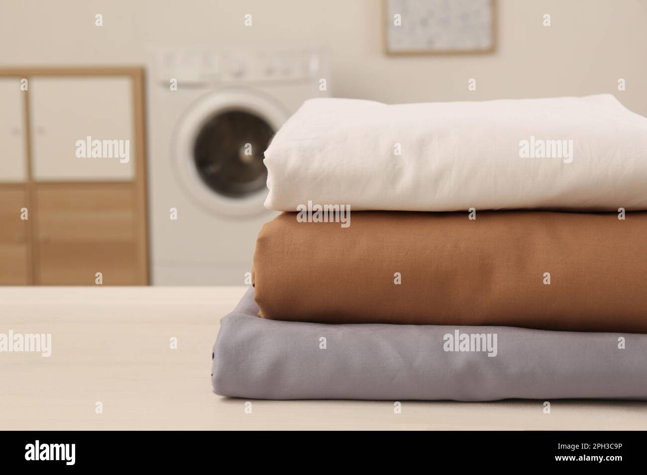 Stack of clean bed linens on white wooden table in laundry room Stock ...