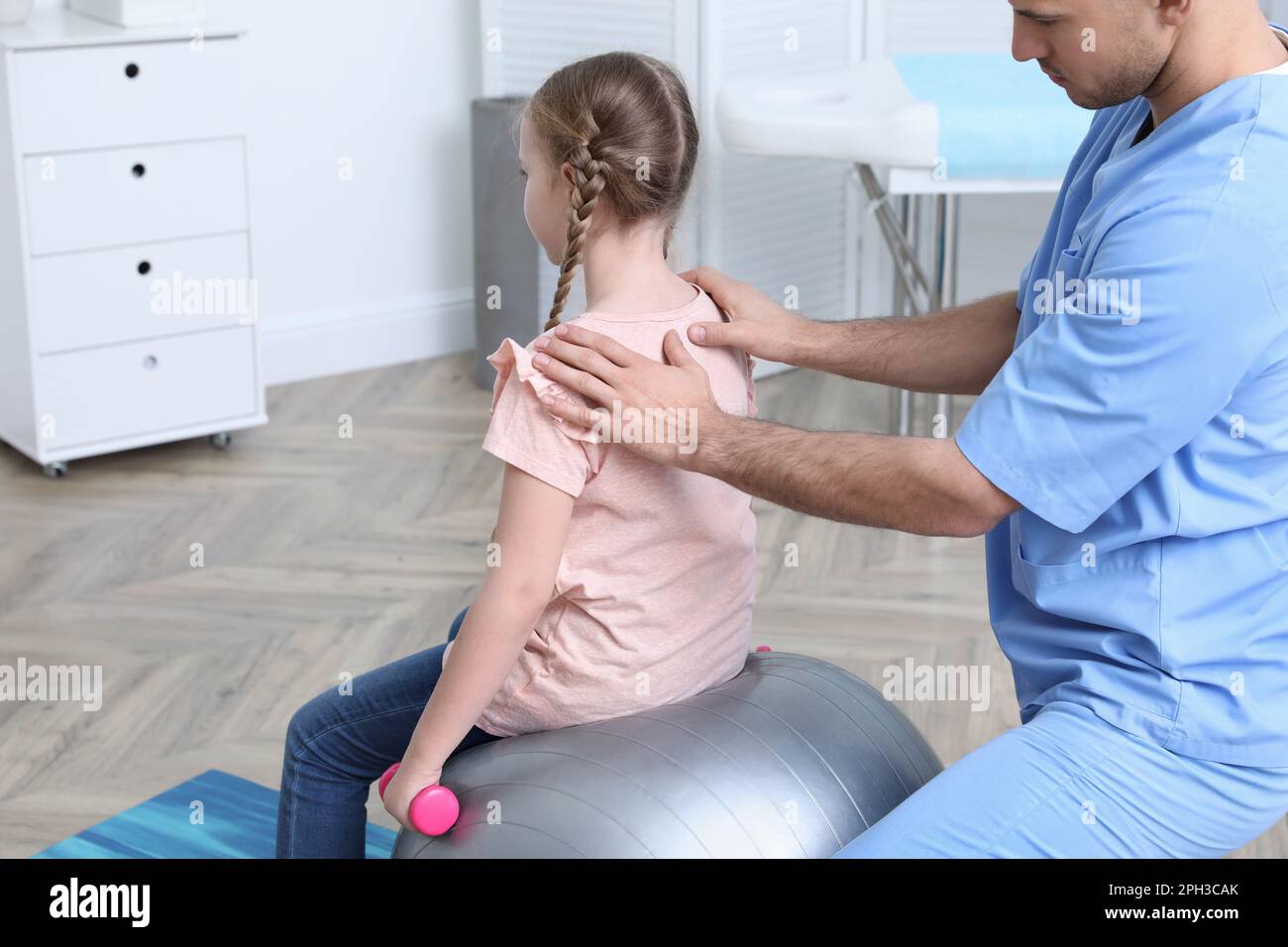 Orthopedist helping child to do exercise with dumbbell in clinic ...