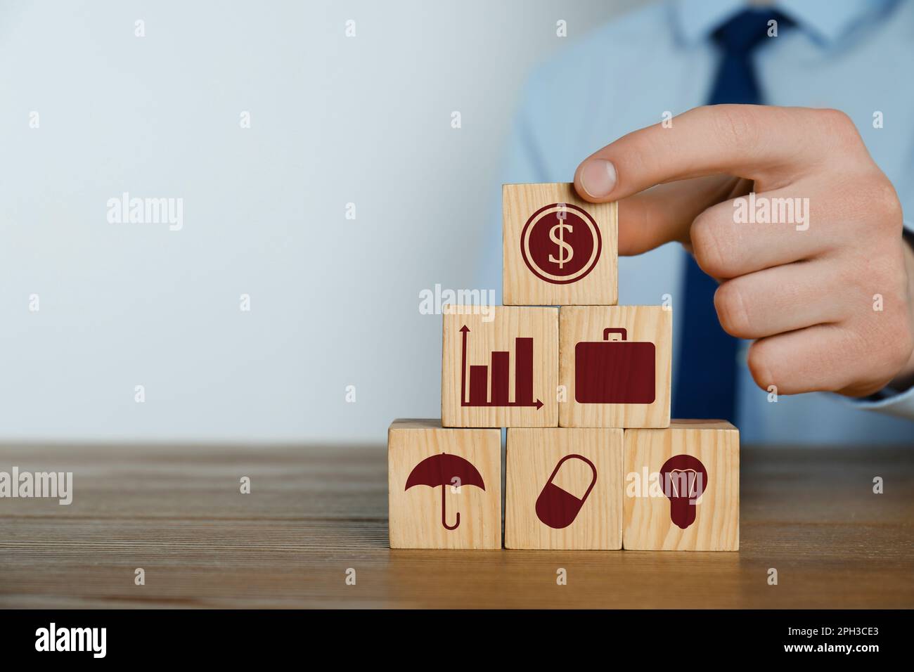 Man building pyramid of cubes with different icons at wooden table ...
