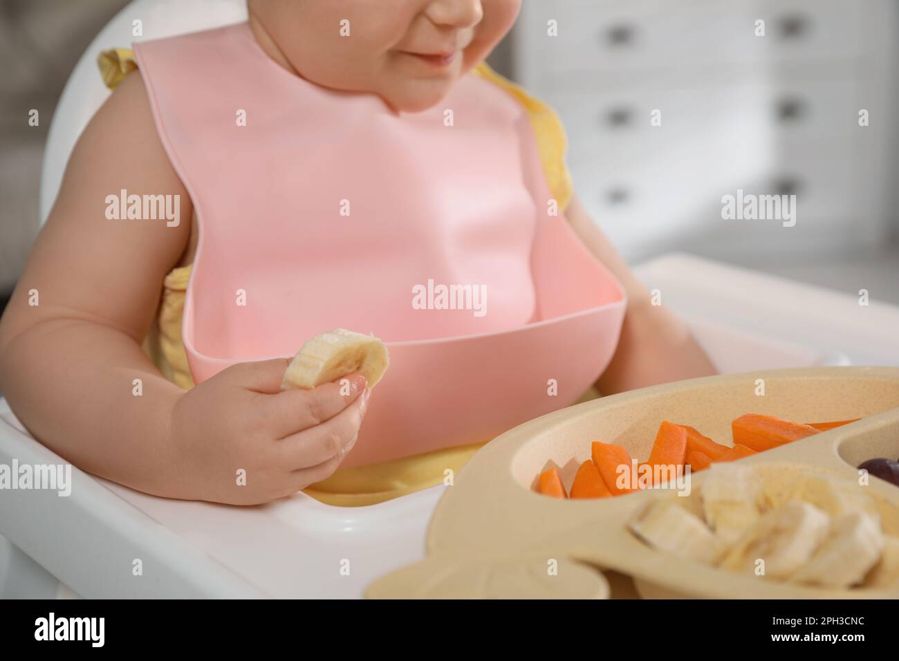 Cute little baby wearing bib while eating at home, closeup Stock Photo ...
