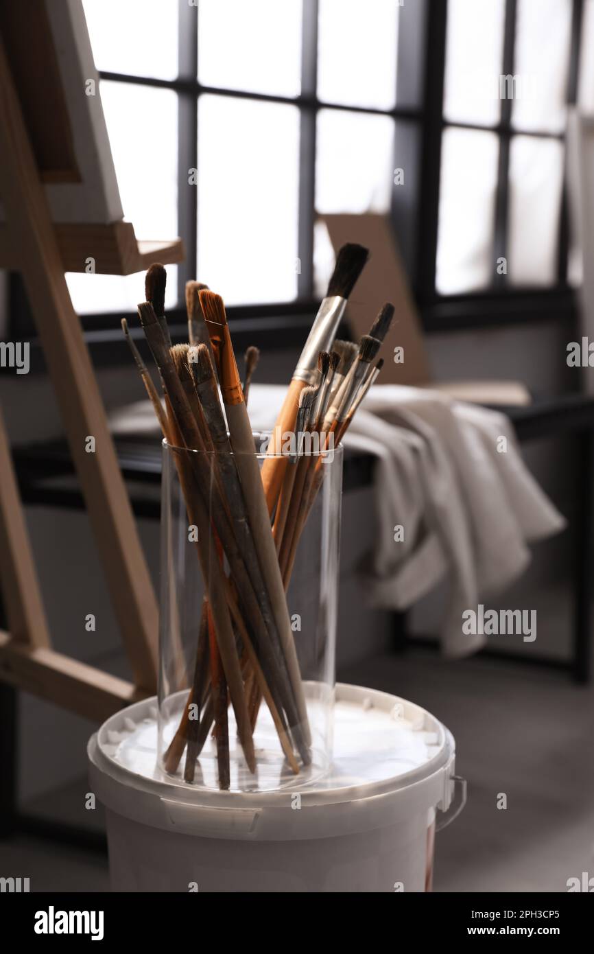 Holder with different brushes on bucket of paint in artist's studio ...