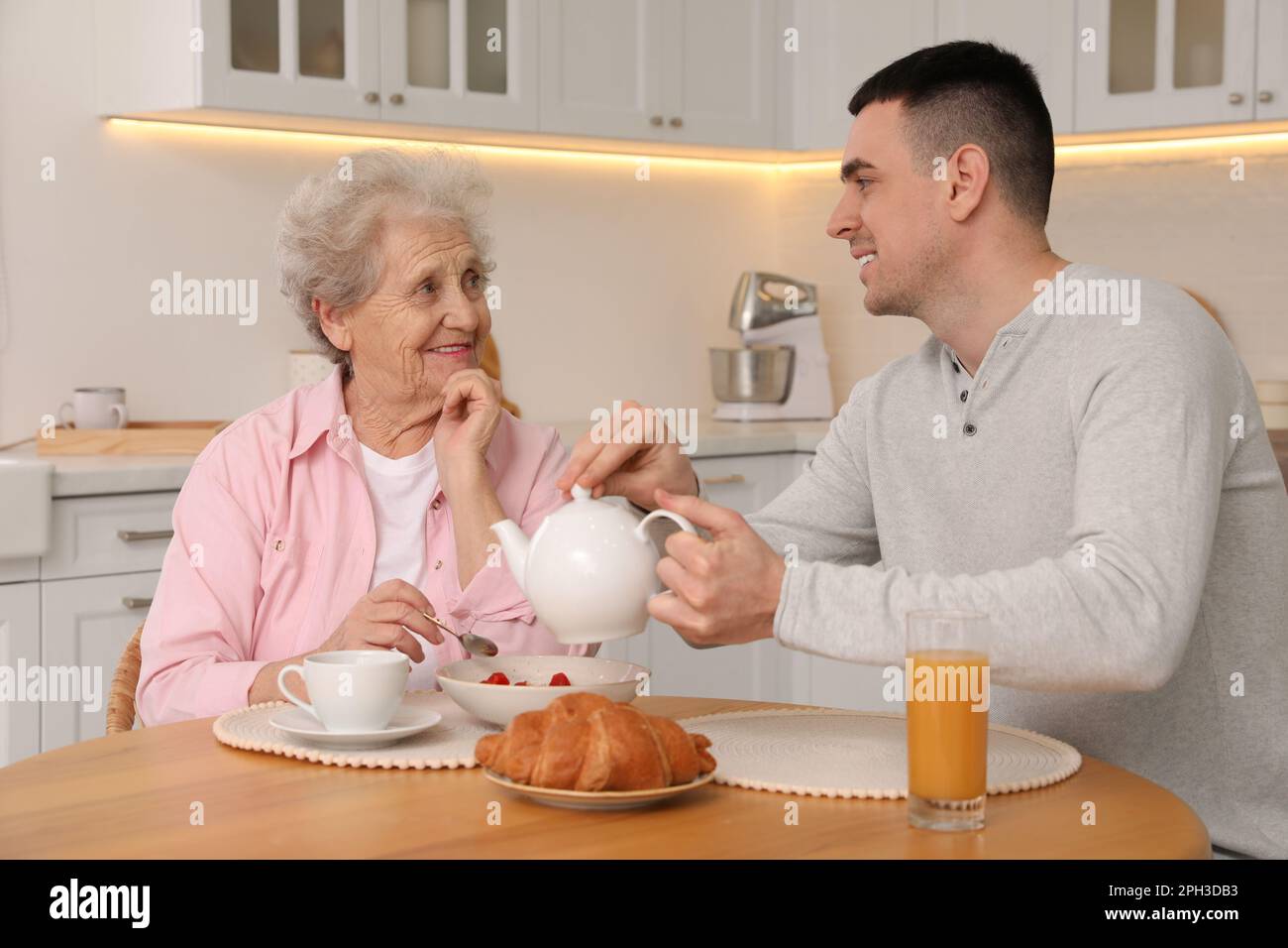 Young caregiver serving breakfast for senior woman at table in kitchen ...