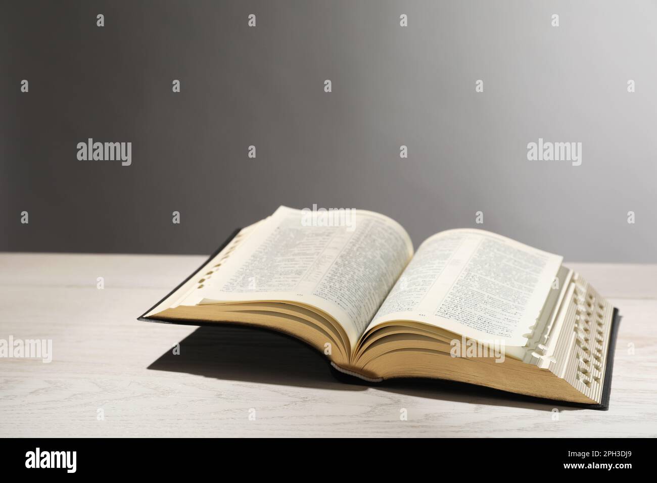 Open Bible on white wooden table against light grey background ...
