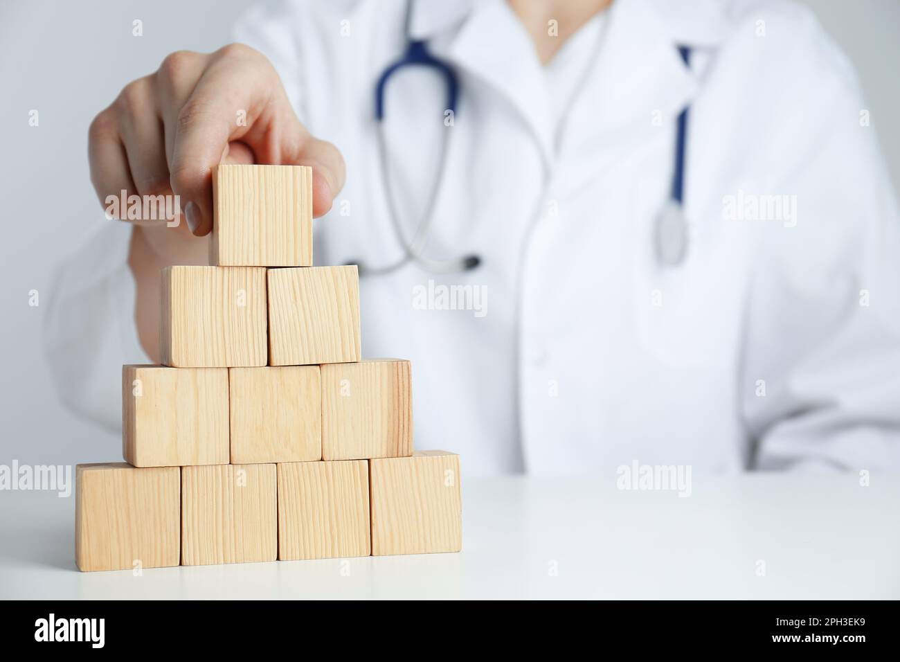 Doctor building pyramid of blank wooden cubes on white table against ...