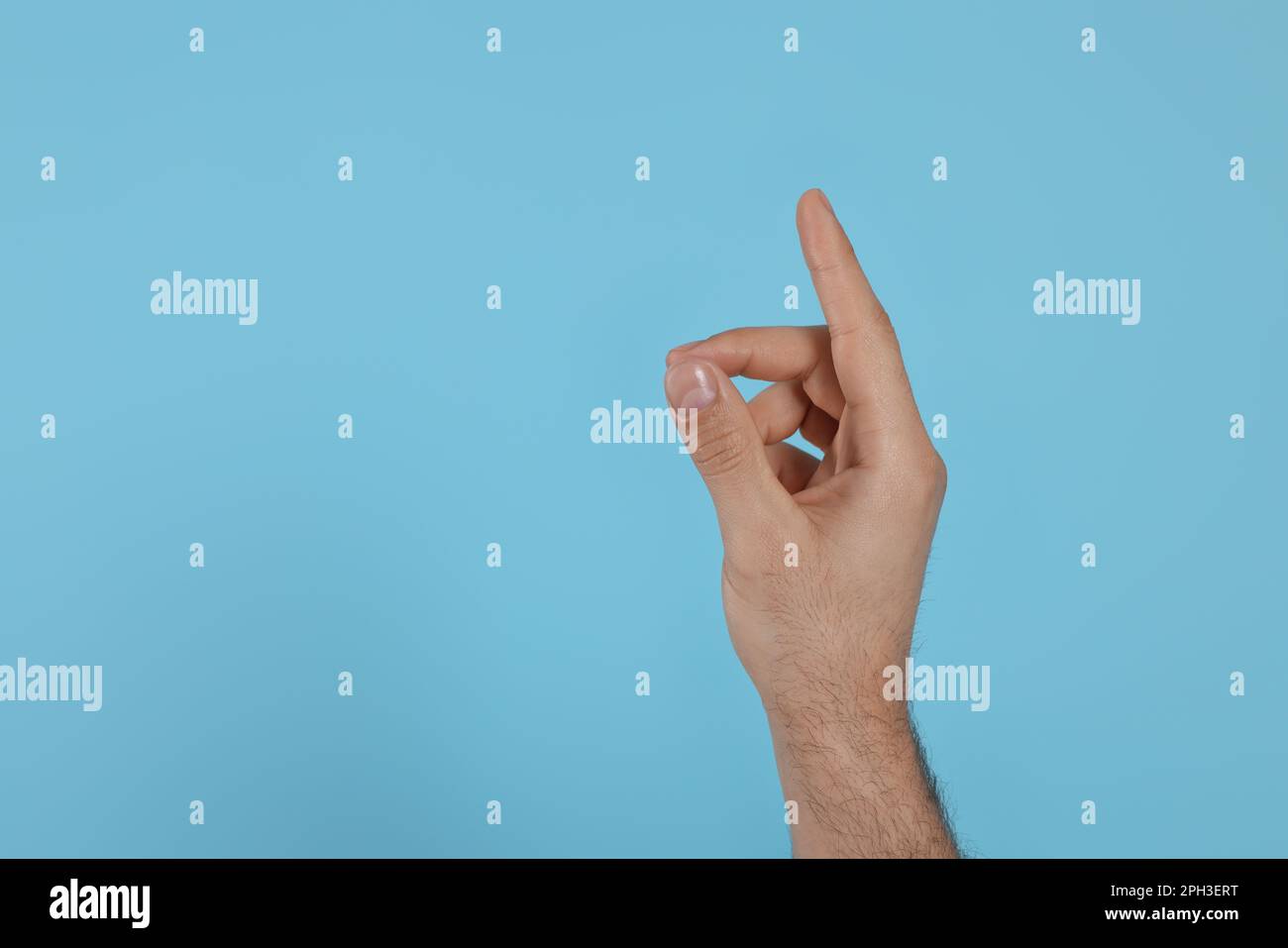 Man pointing at something on light blue background, closeup of hand ...