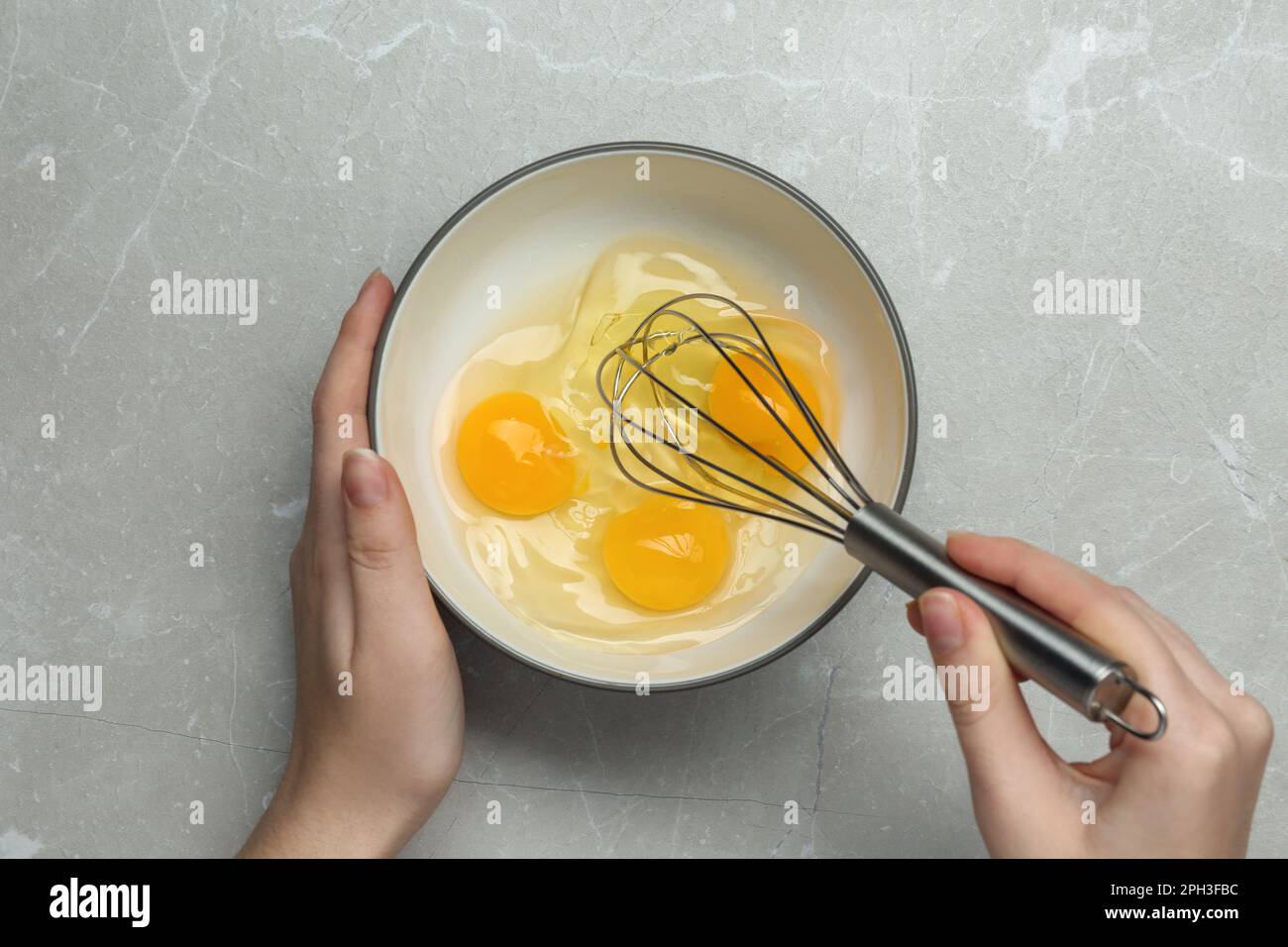 Woman whisking eggs in bowl at light grey table, top view Stock Photo ...