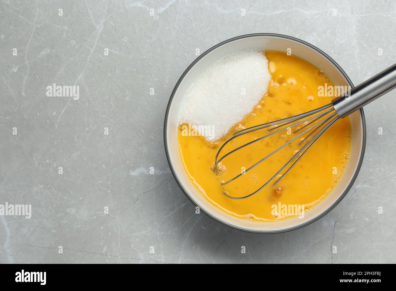 Bowl with whisked eggs and sugar on light grey table, top view. Space ...