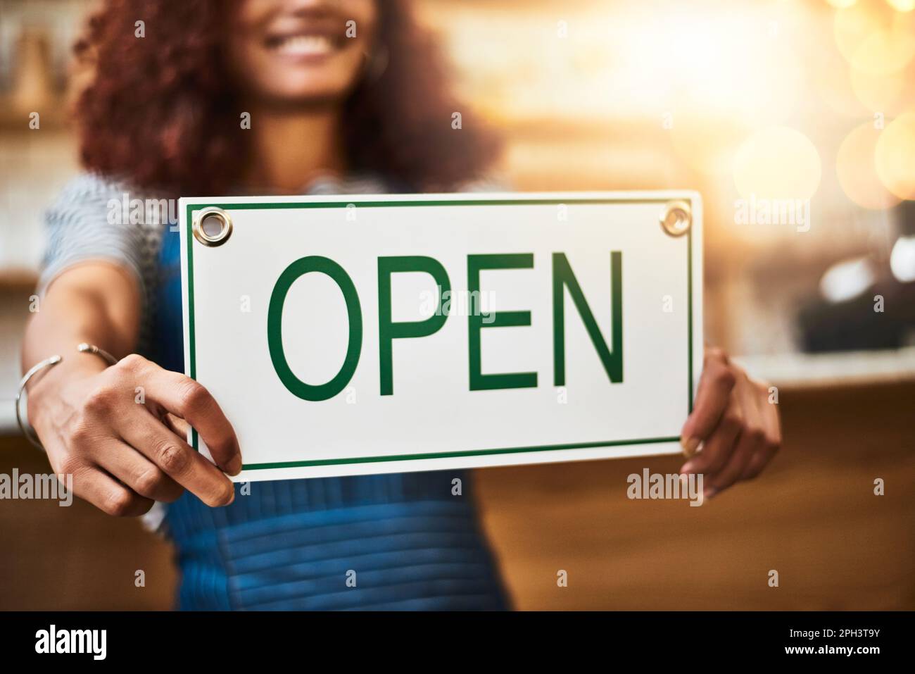 Please do come on in. a young woman holding up an open sign in her ...