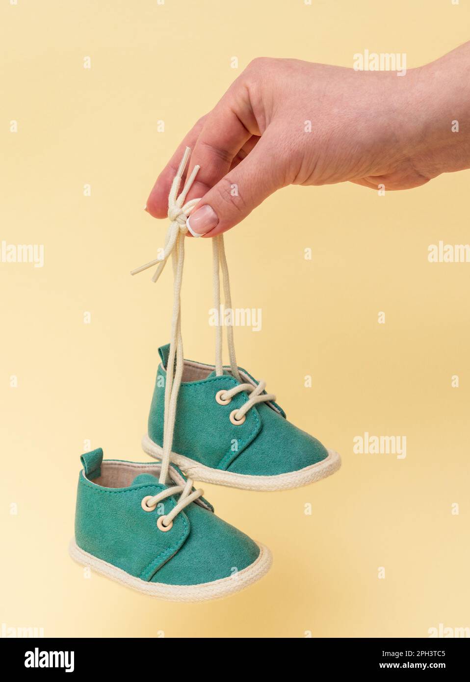 Woman holding newborn baby tiny shoes with laces on yellow background ...