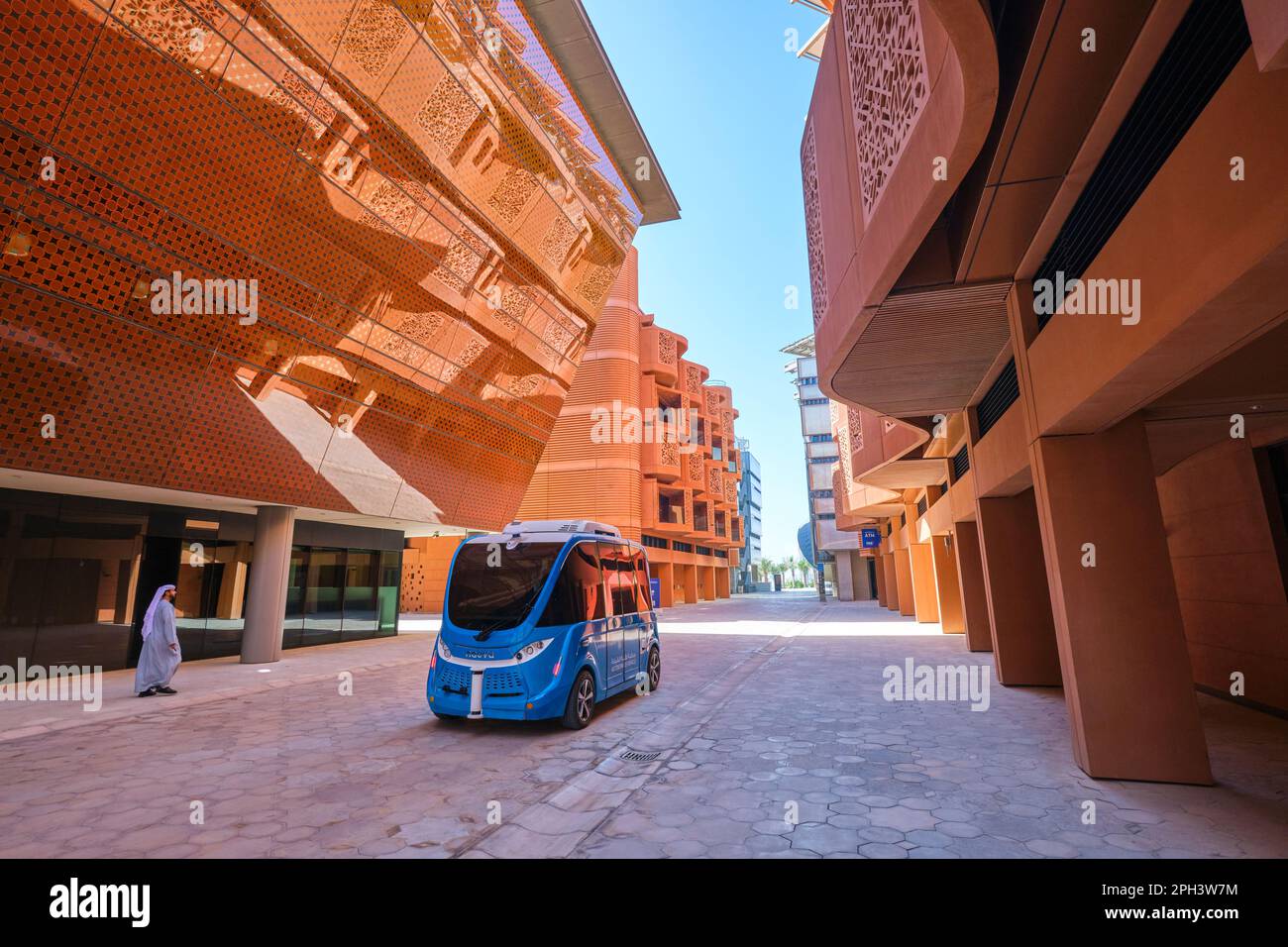 Orange terracotta clad mixed use apartments with blue, electric transport vehicle. At Masdar ...