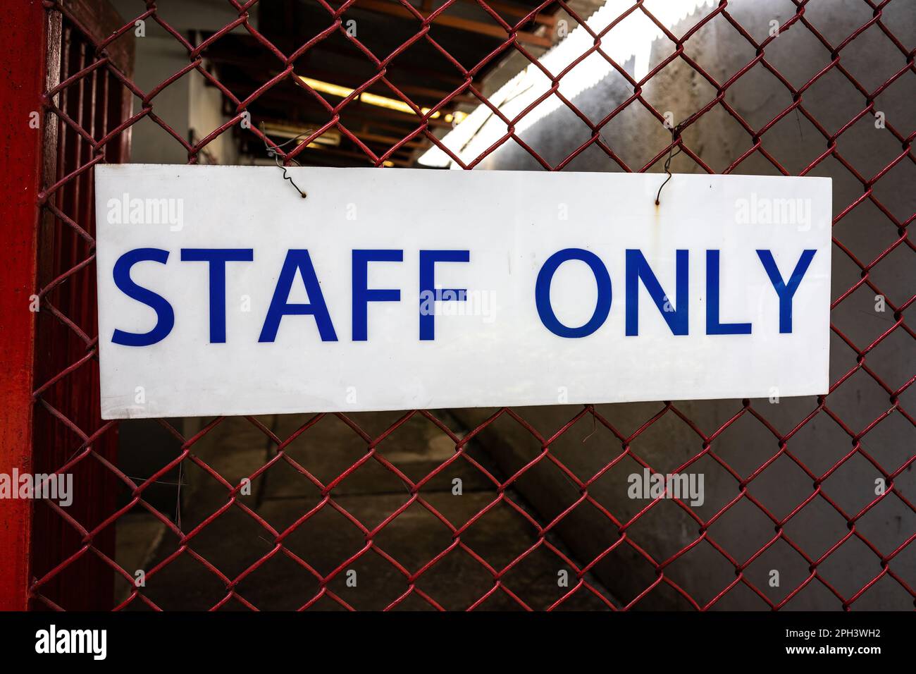 White sign in front of a red metal fence reading 'staff only' in blue ...