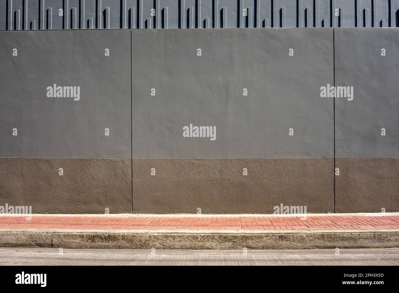 Frontal view of a black wall with a red brick sidewalk in daytime with ...