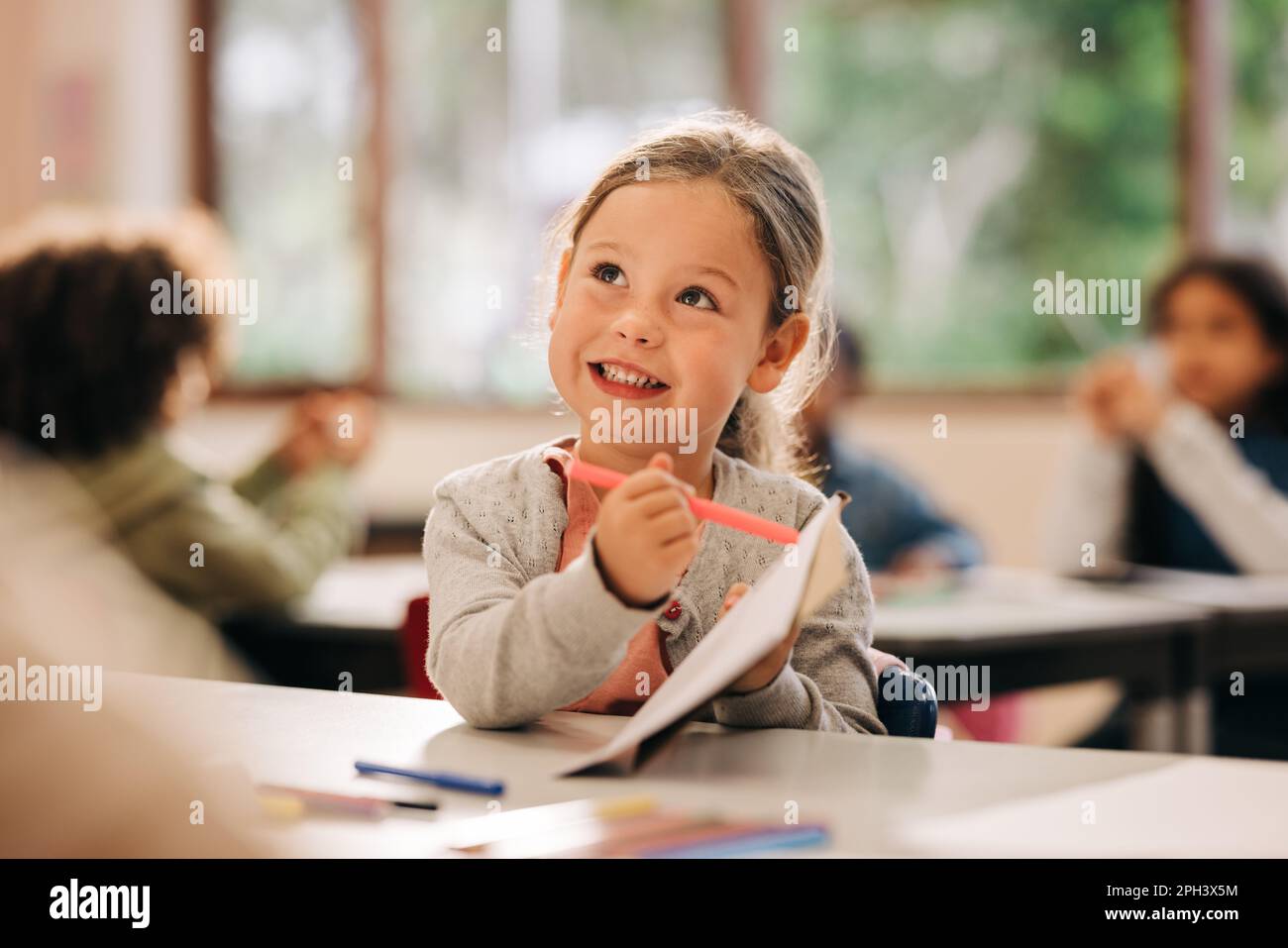 Excited little girl learns to draw with a colour pencil in an art class ...