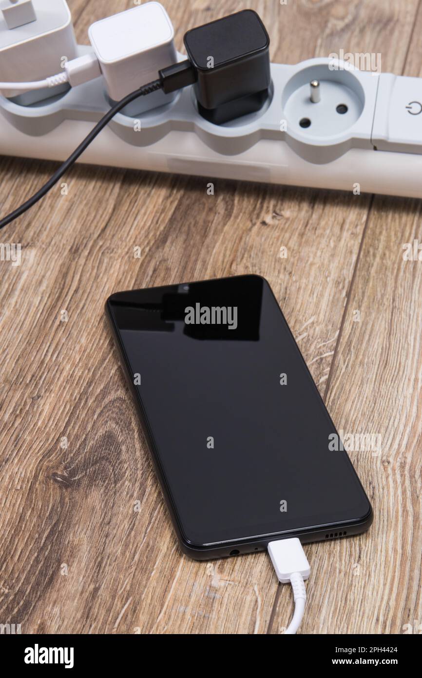 Black smartphone, mobile phone and chargers connected to electrical ...