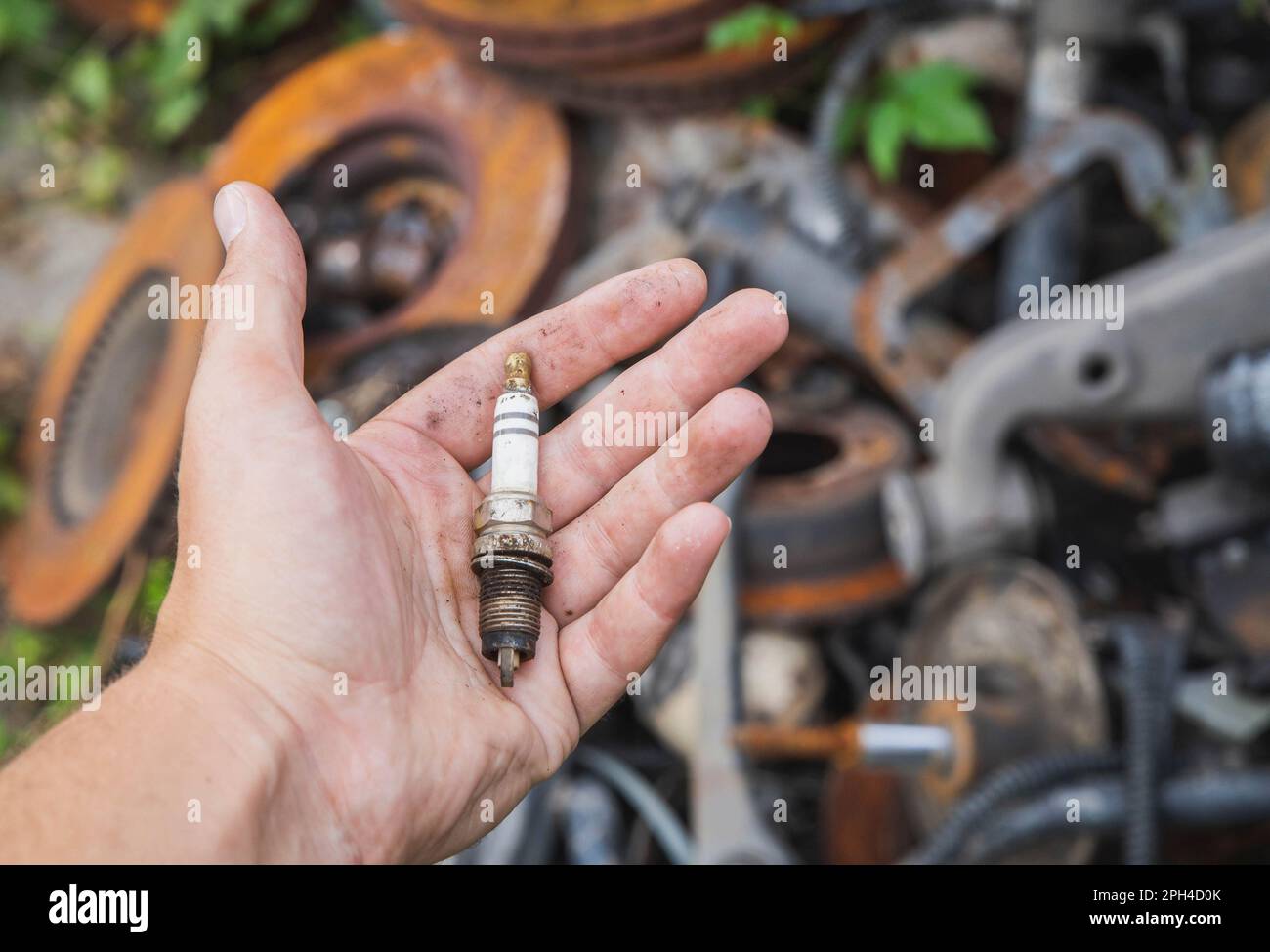 old spark plug in hand near a pile of rusty spare parts in a landfill ...