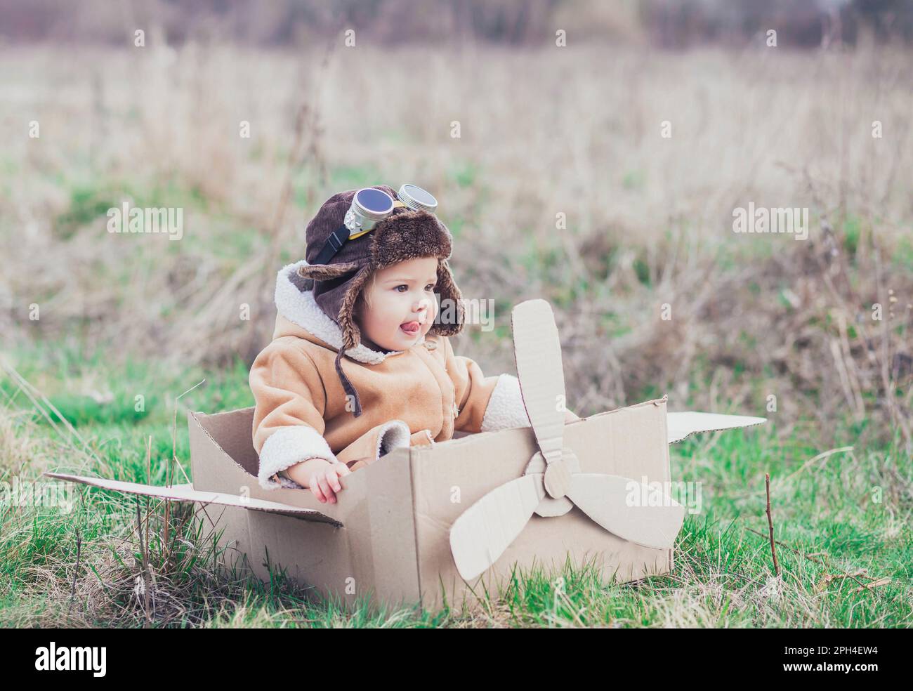 Charming baby in a cardboard homemade plane imagines that he is flying ...