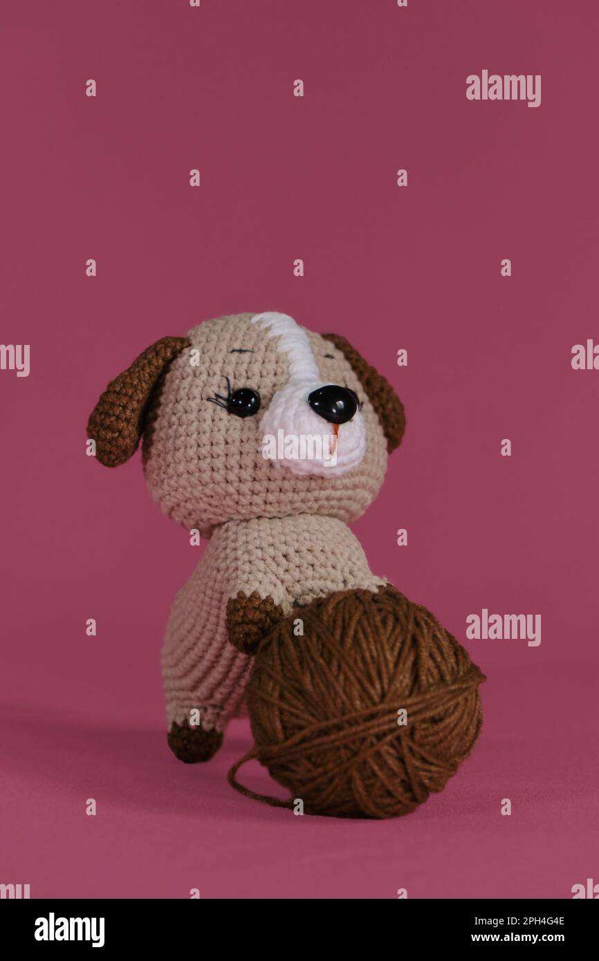Amigurumi doll puppy on pink background playing with ball of thread. A ...