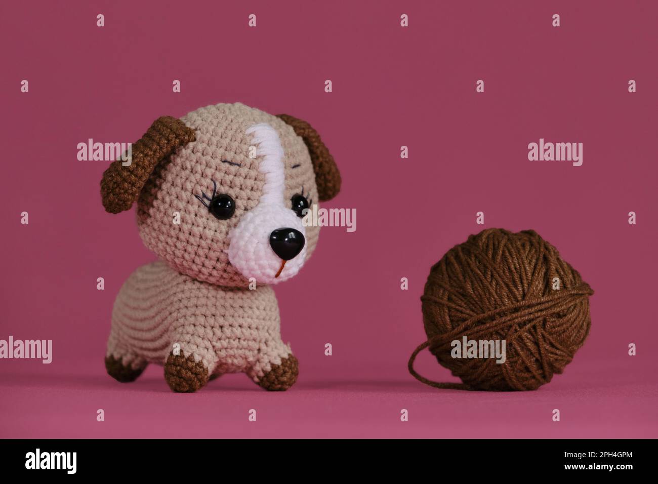 Amigurumi puppy doll on pink background next to ball of thread. Soft ...