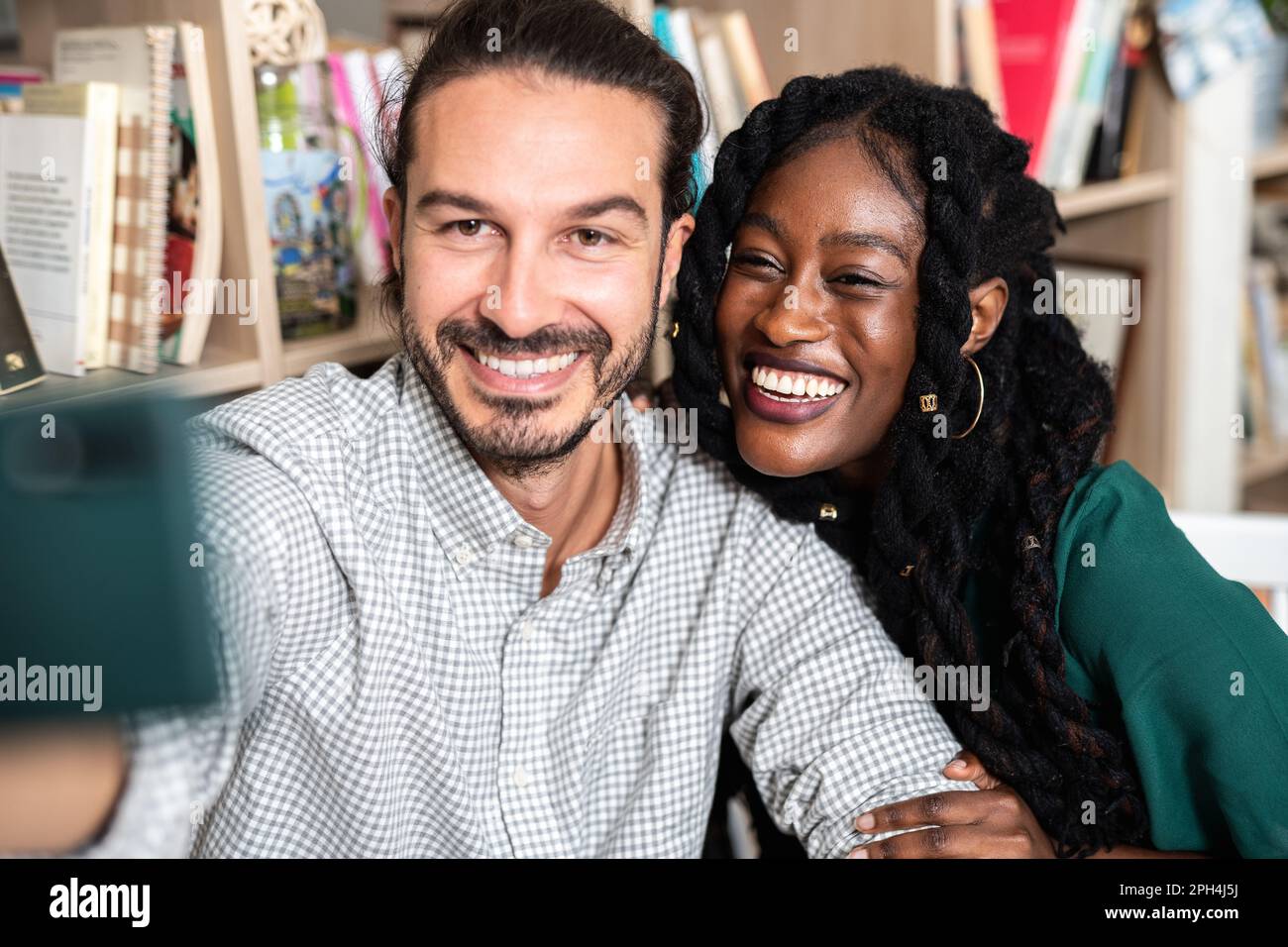 A multicultural couple taking a selfie in a library, enjoying each ...