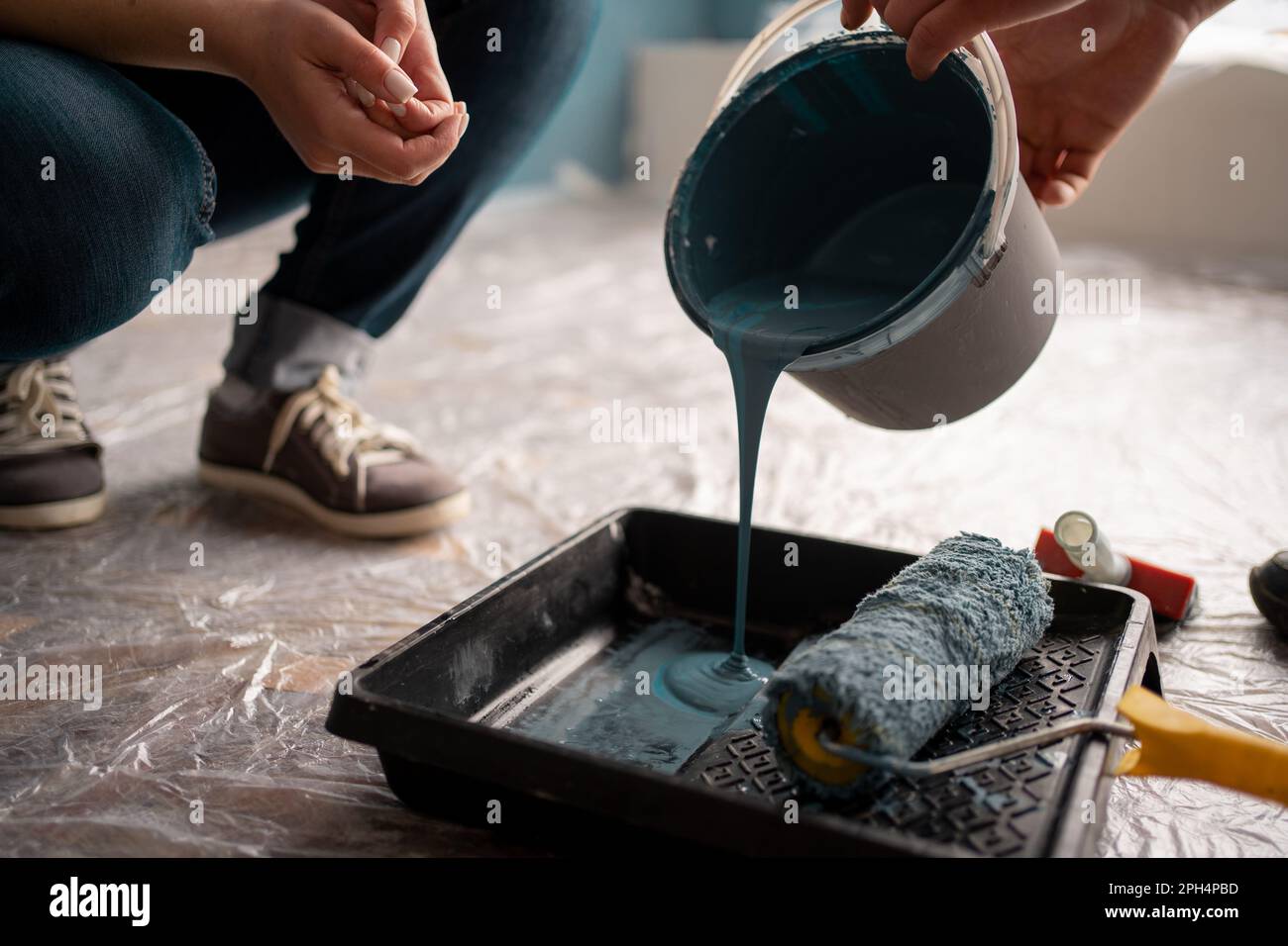 Young man picks up a can of dark blue paint and pours it into a tray ...