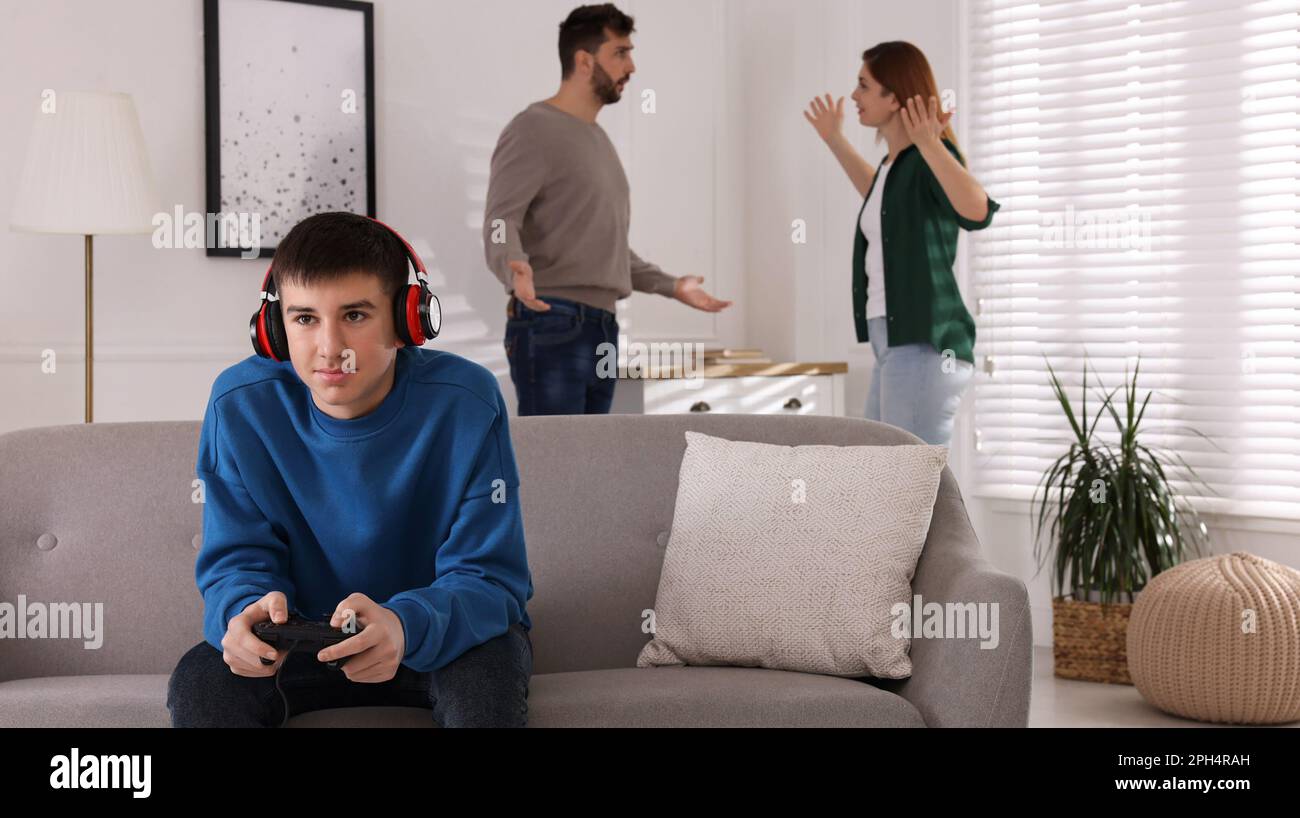 Teenage boy playing videogame while his parents arguing on background ...