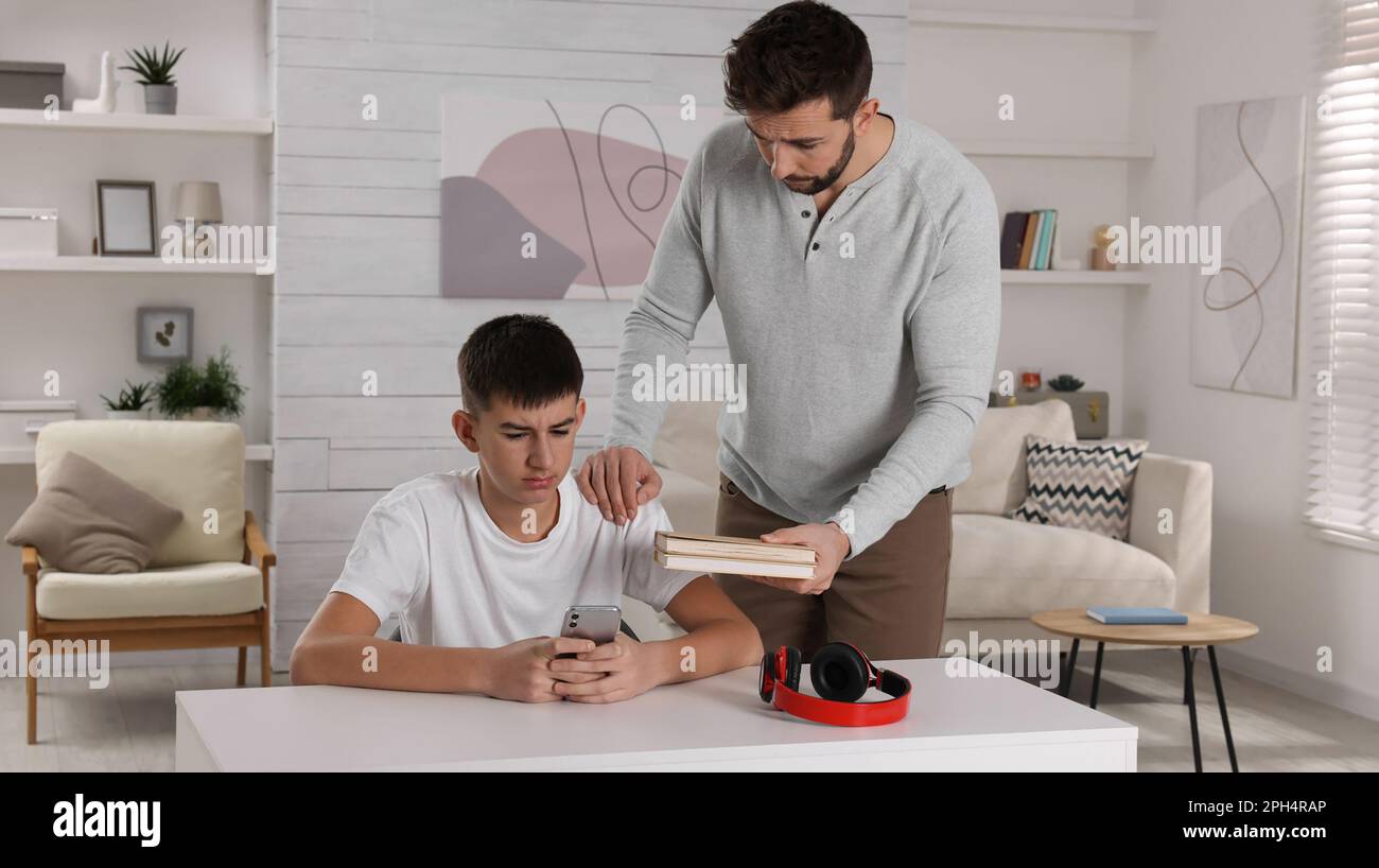 Strict father with books scolding his son while he using smartphone at ...