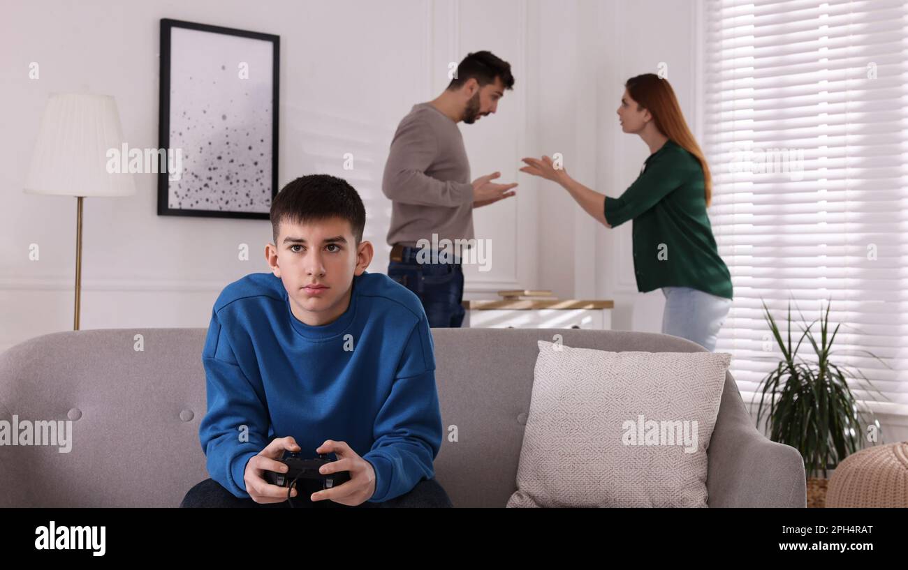 Teenage boy playing videogame while his parents arguing on background ...
