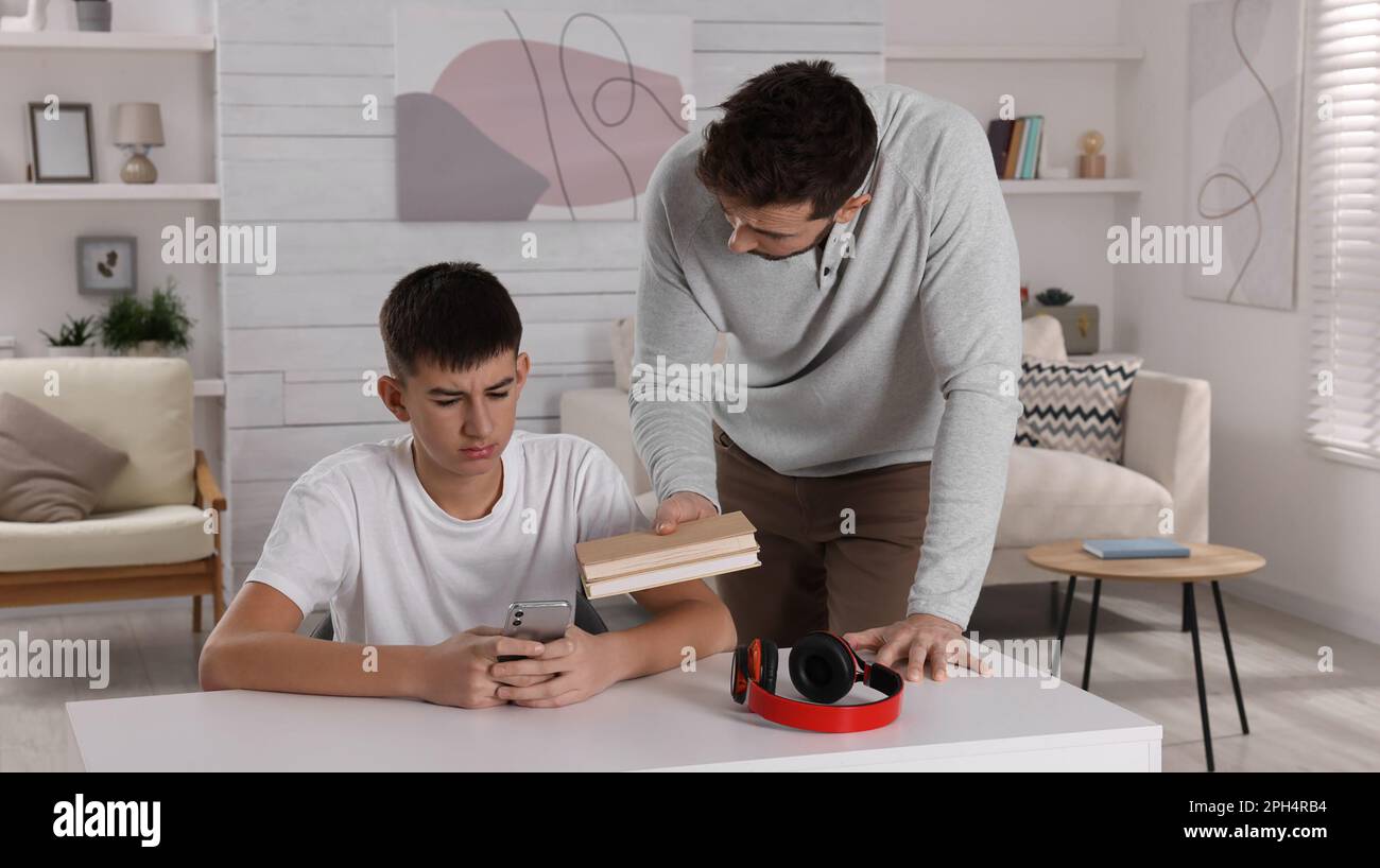 Strict father with books scolding his son while he using smartphone at ...