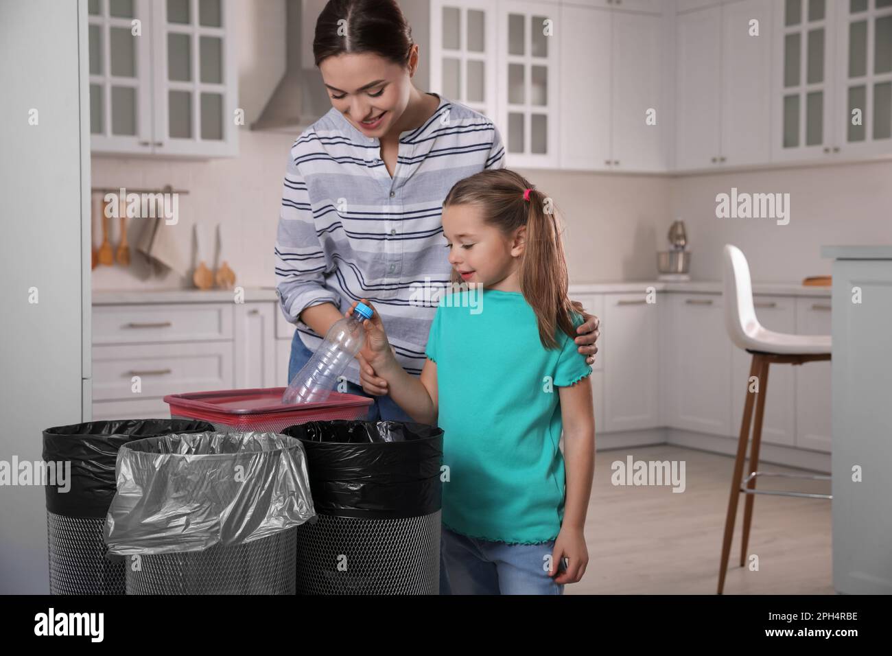 Young woman and her daughter throwing plastic bottle into trash bin in ...