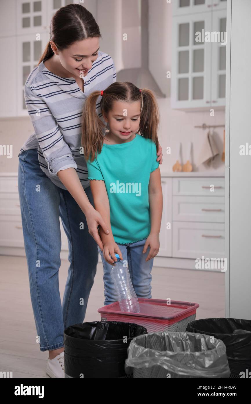 Young woman and her daughter throwing plastic bottle into trash bin in ...