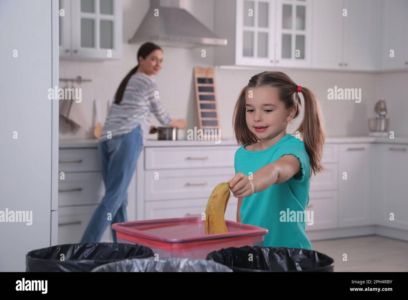 Little girl throwing banana peel into trash bin in kitchen. Separate ...