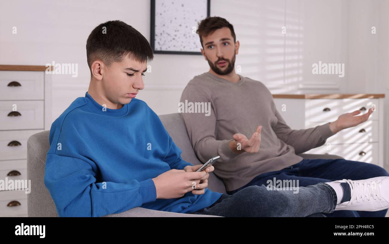Boy using smartphone and ignoring his upset father at home. Teenager ...