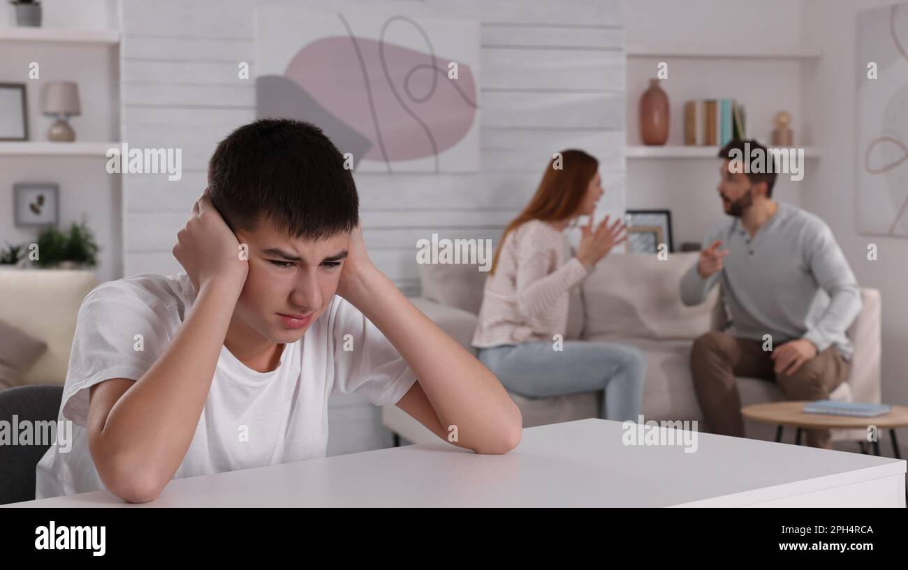 Unhappy teenage boy covering ears while his parents arguing on ...