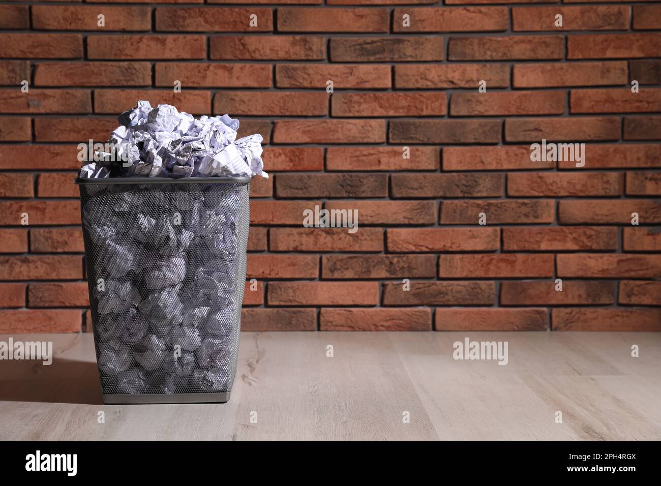Trash bin full of paper on floor near brick wall, space for text ...