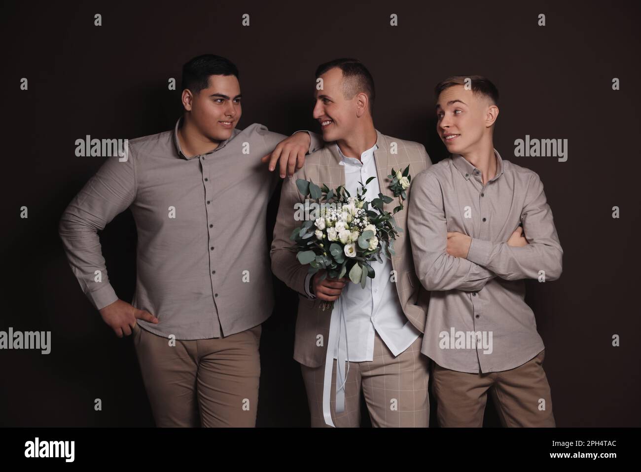 Happy groom with bouquet and his groomsmen on brown background Stock ...