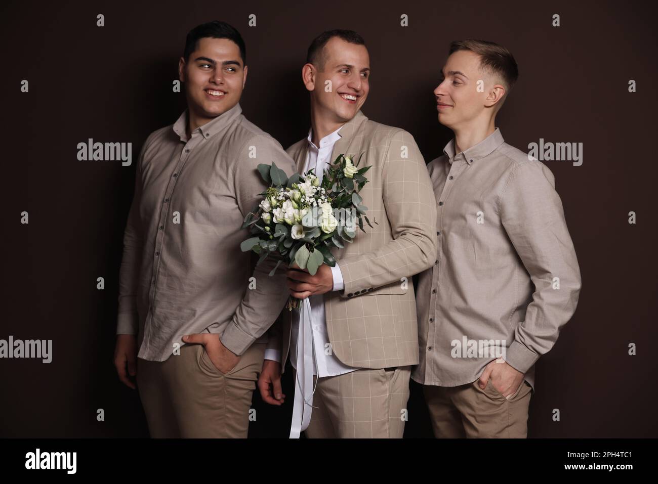 Happy groom with bouquet and his groomsmen on brown background Stock ...