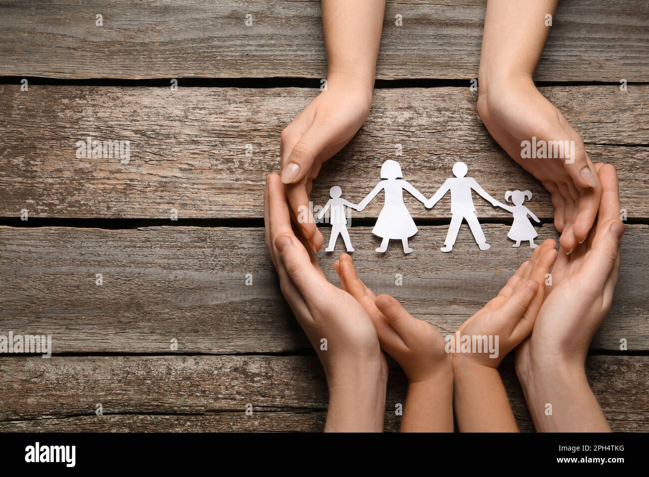 Parents and child protecting paper cutout of family at wooden table ...
