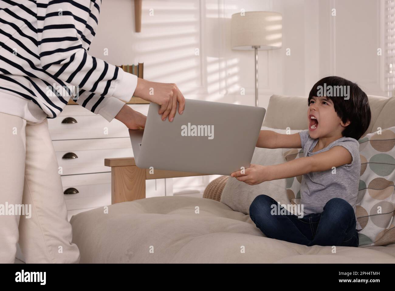 Internet addiction. Woman taking laptop from her angry son in living ...
