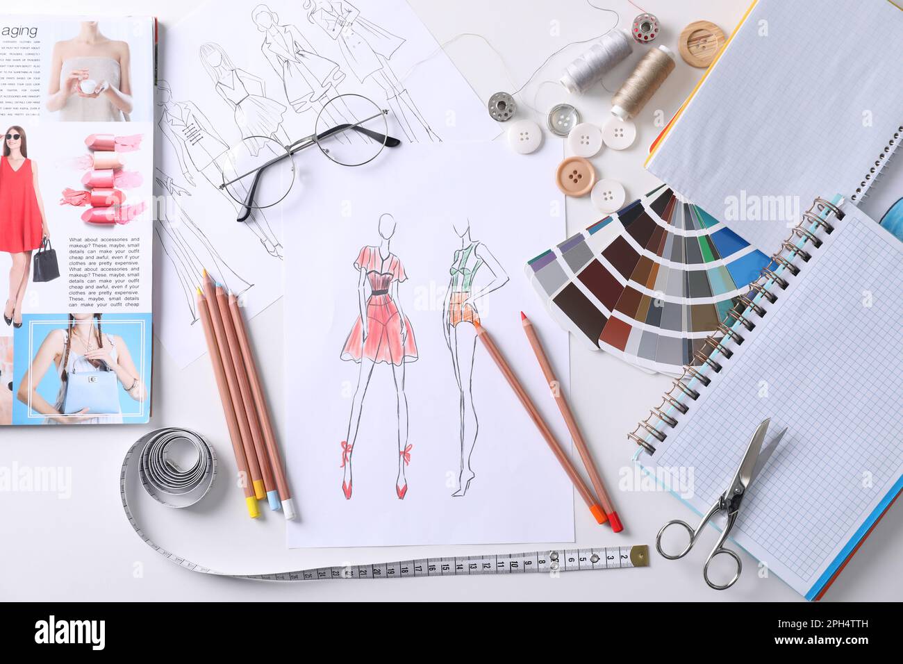 Sketches of clothes and different stuff on white table, flat lay. Fashion designer's workplace ...