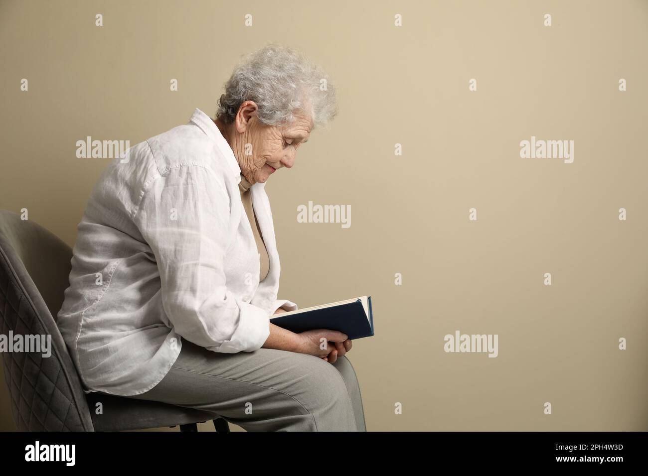Elderly woman with poor posture reading book on beige background. Space ...