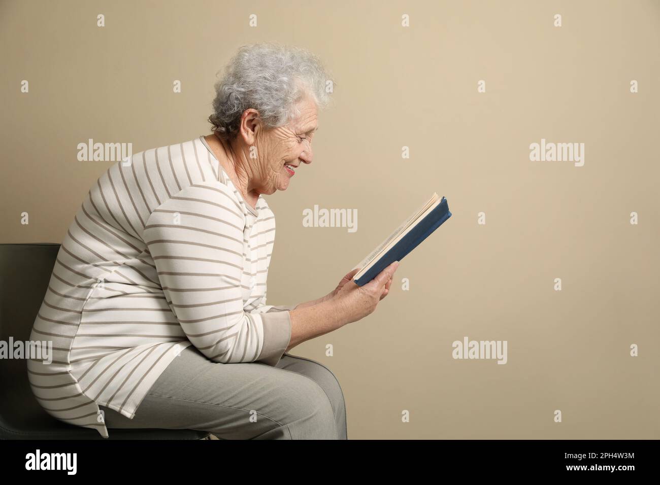 Elderly woman with poor posture reading book on beige background Stock ...