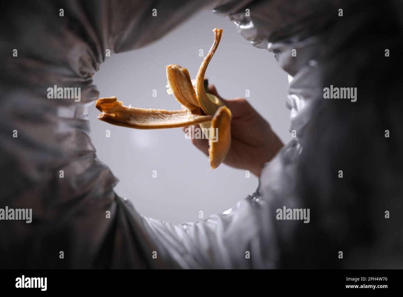 Bottom view of woman throwing banana peel into trash bin on grey ...