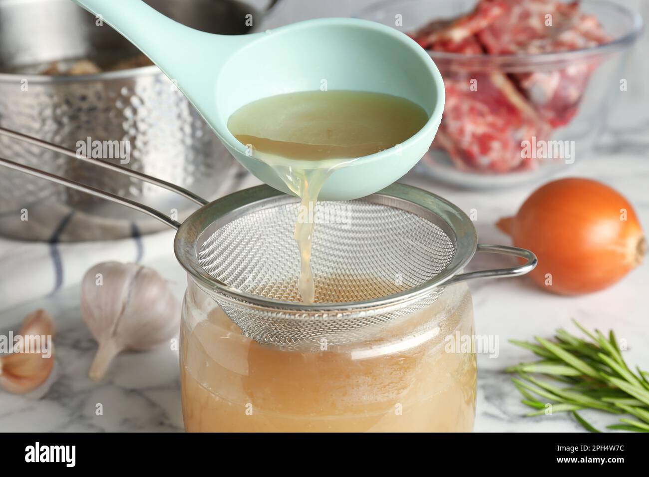 Straining delicious broth through sieve on white marble table, closeup ...