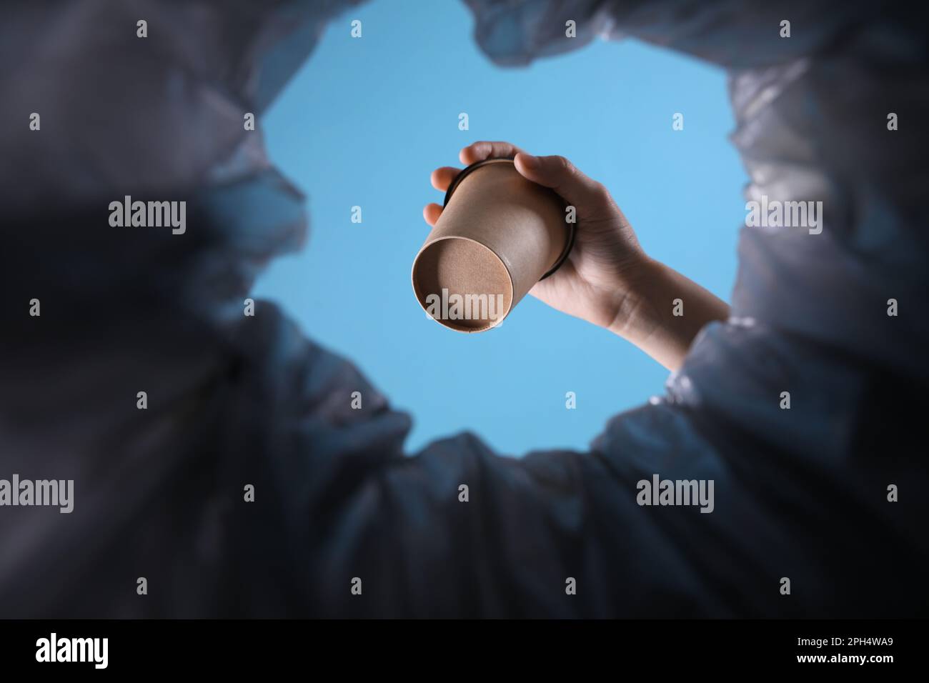 Bottom view of woman throwing paper cup into trash bin on light blue ...