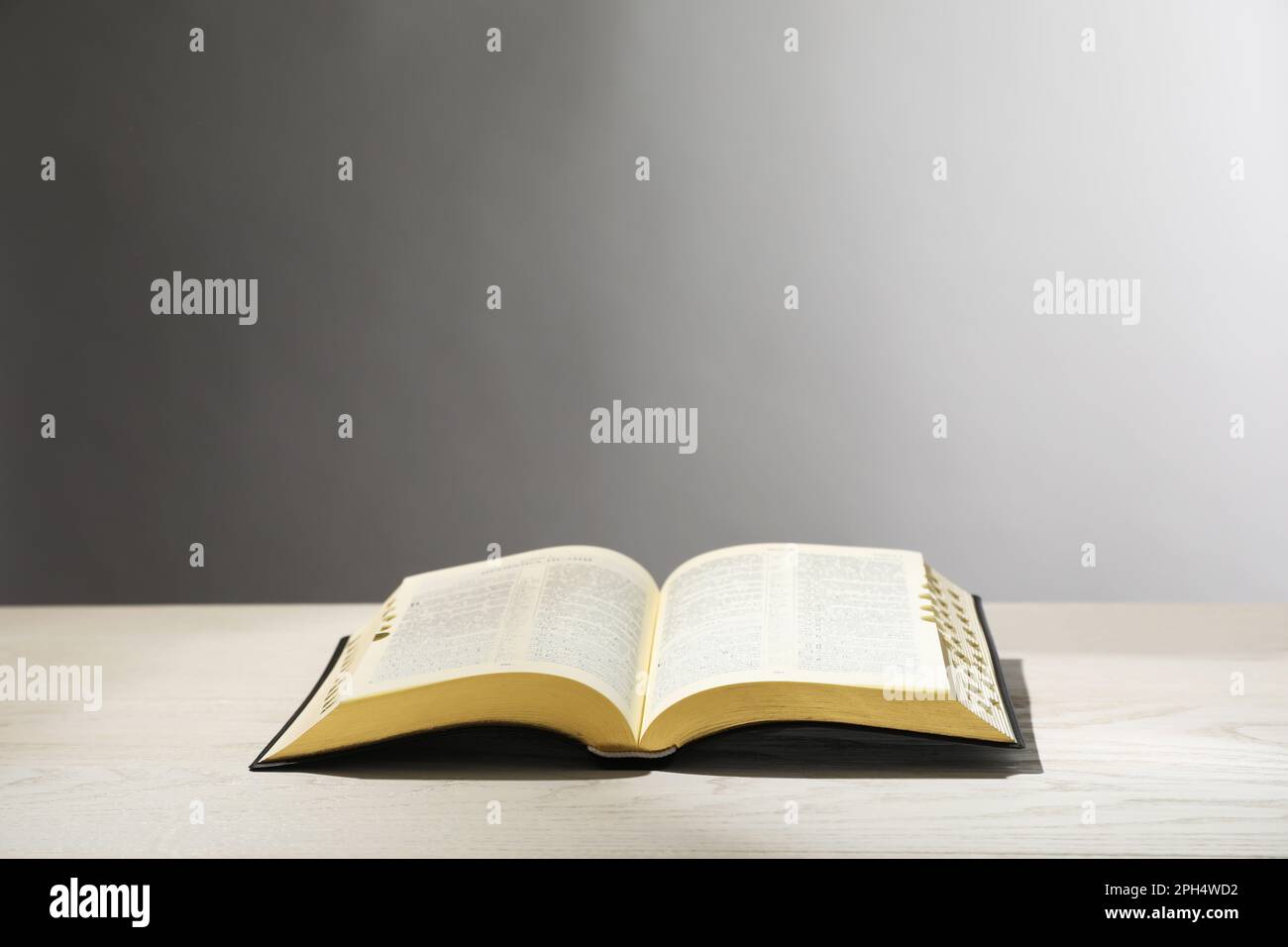 Open Bible on white wooden table against light grey background ...