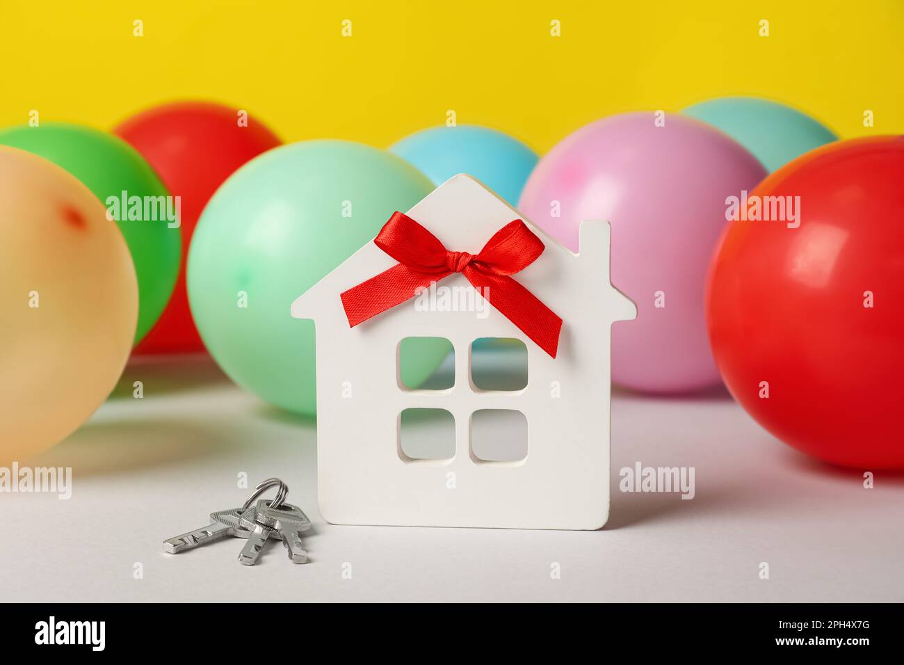 House model with red bow, keys and colorful balloons on white table ...
