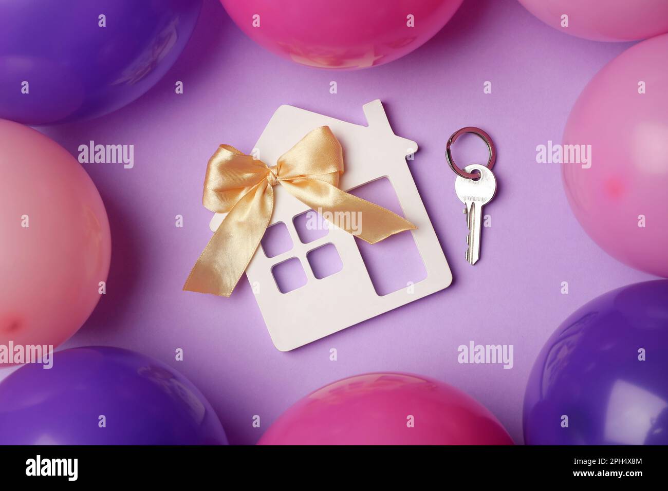 House model with bow, key and colorful balloons on violet background ...